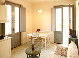 Cozinha compacta com área de refeições, uma mesa pequena com cadeiras, uma mesinha de vime e um sofá com almofadas florais.