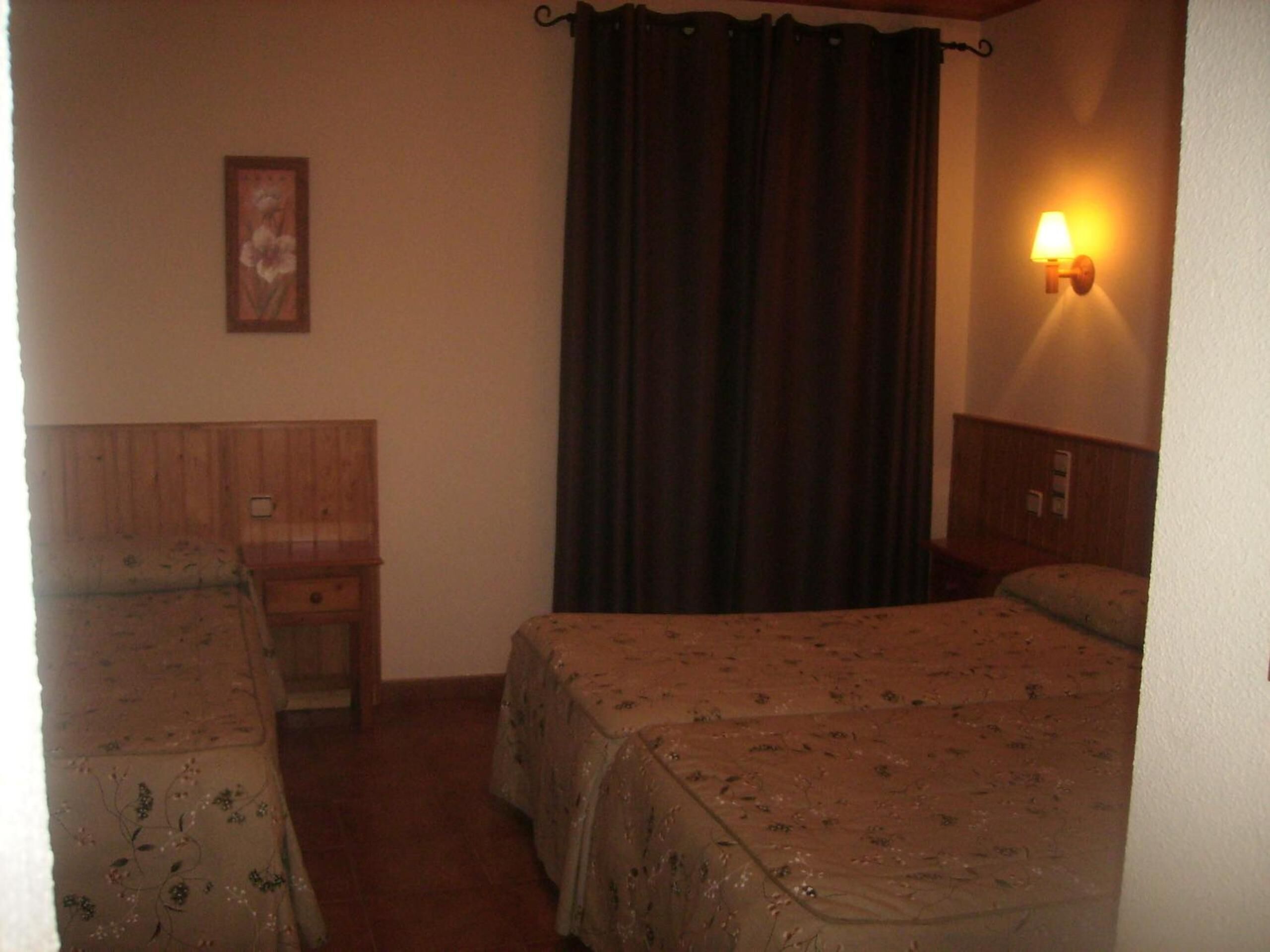 Quarto com duas camas, cabeceira de madeira, mesa de cabeceira, luminária na parede e um quadro emoldurado.