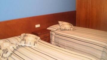 Quarto com duas camas, cada uma com roupa de cama listrada e um travesseiro. Possui cabeceira de madeira e uma pequena mesa de cabeceira com uma luminária.