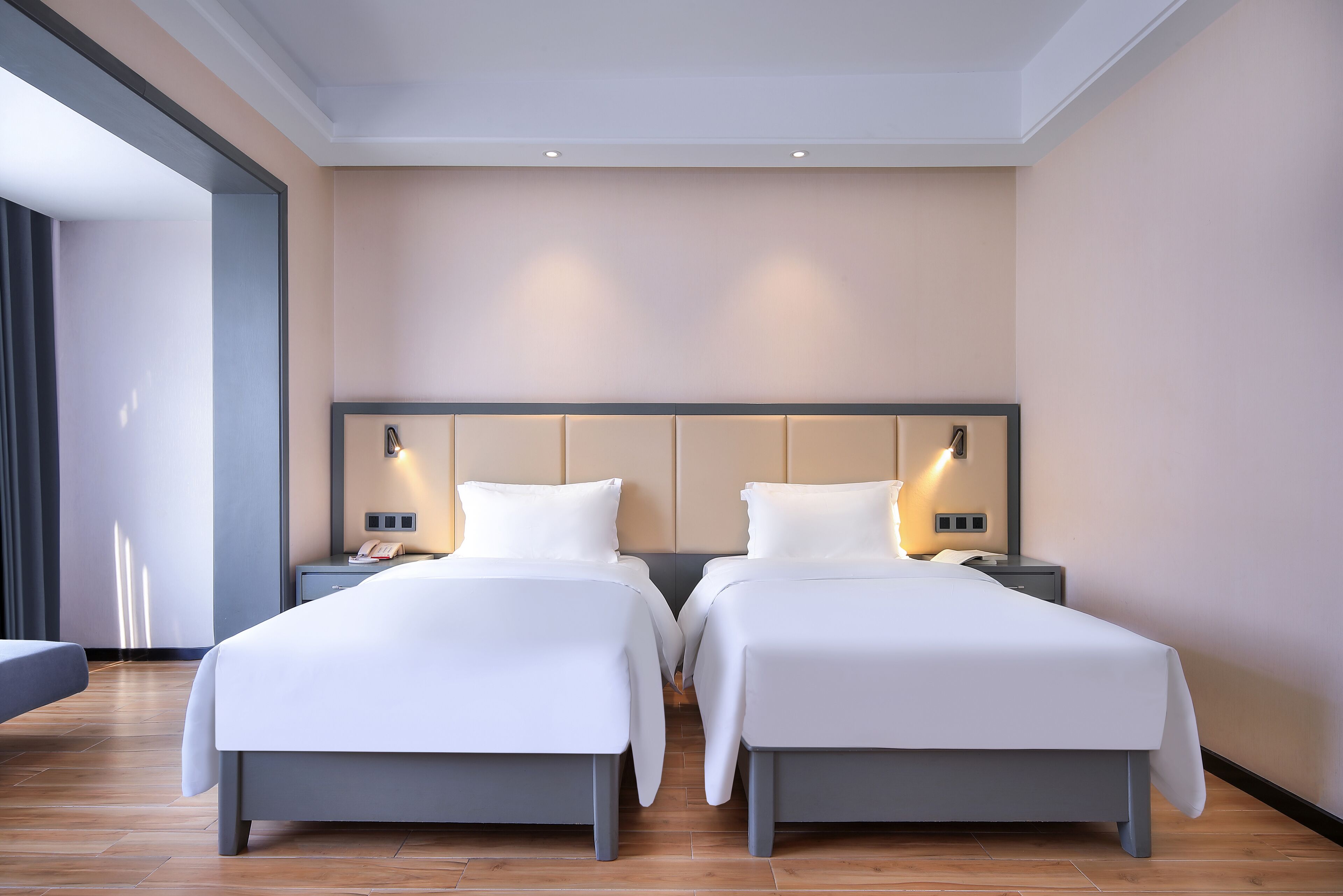 Quarto de hotel moderno com duas camas, paleta de cores neutras e iluminação embutida.
