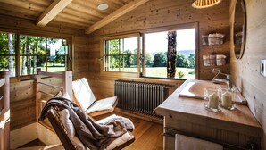 Interior de uma cabana de madeira com uma cama, uma janela com vista para árvores, uma pia e um espelho.
