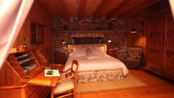 Um quarto de cabana de madeira acolhedor, com parede de pedra, uma cama com roupa de cama floral, uma escrivaninha de madeira com livros e uma cadeira.
