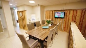 Uma sala de jantar com uma mesa de madeira, cadeiras de vime e uma televisão na parede.