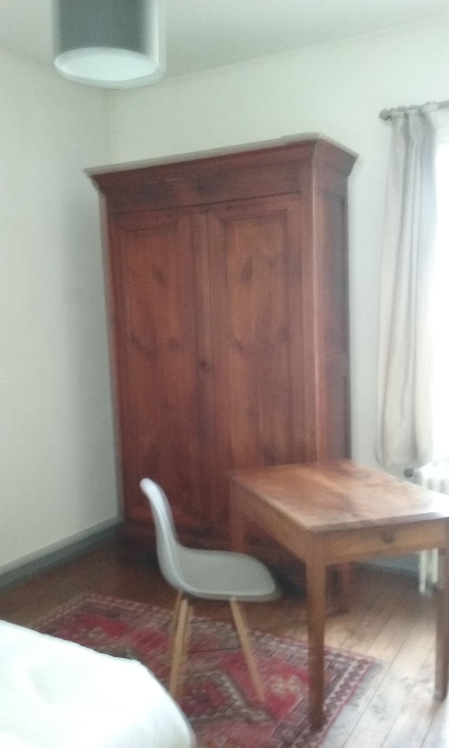 Quarto com um armário de madeira, uma cadeira branca e uma mesa pequena.