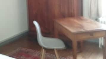 Quarto com um armário de madeira, uma cadeira branca e uma mesa pequena.