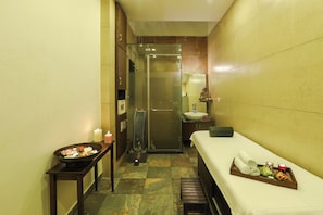 Quarto de hotel pequeno e compacto, com chuveiro, pia e cama com bandeja de toalhas e produtos de higiene.
