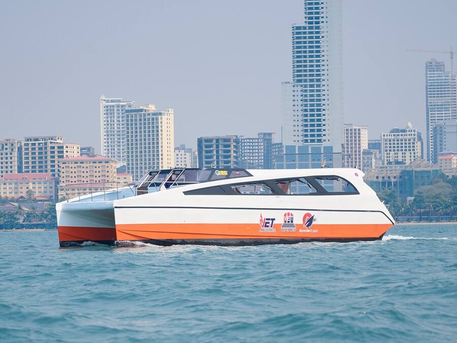 Um barco rápido com design aerodinâmico, navegando em águas com um horizonte urbano ao fundo.