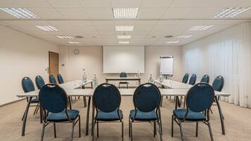 Sala de conferências com uma mesa comprida, cadeiras, tela de projetor e um relógio na parede.