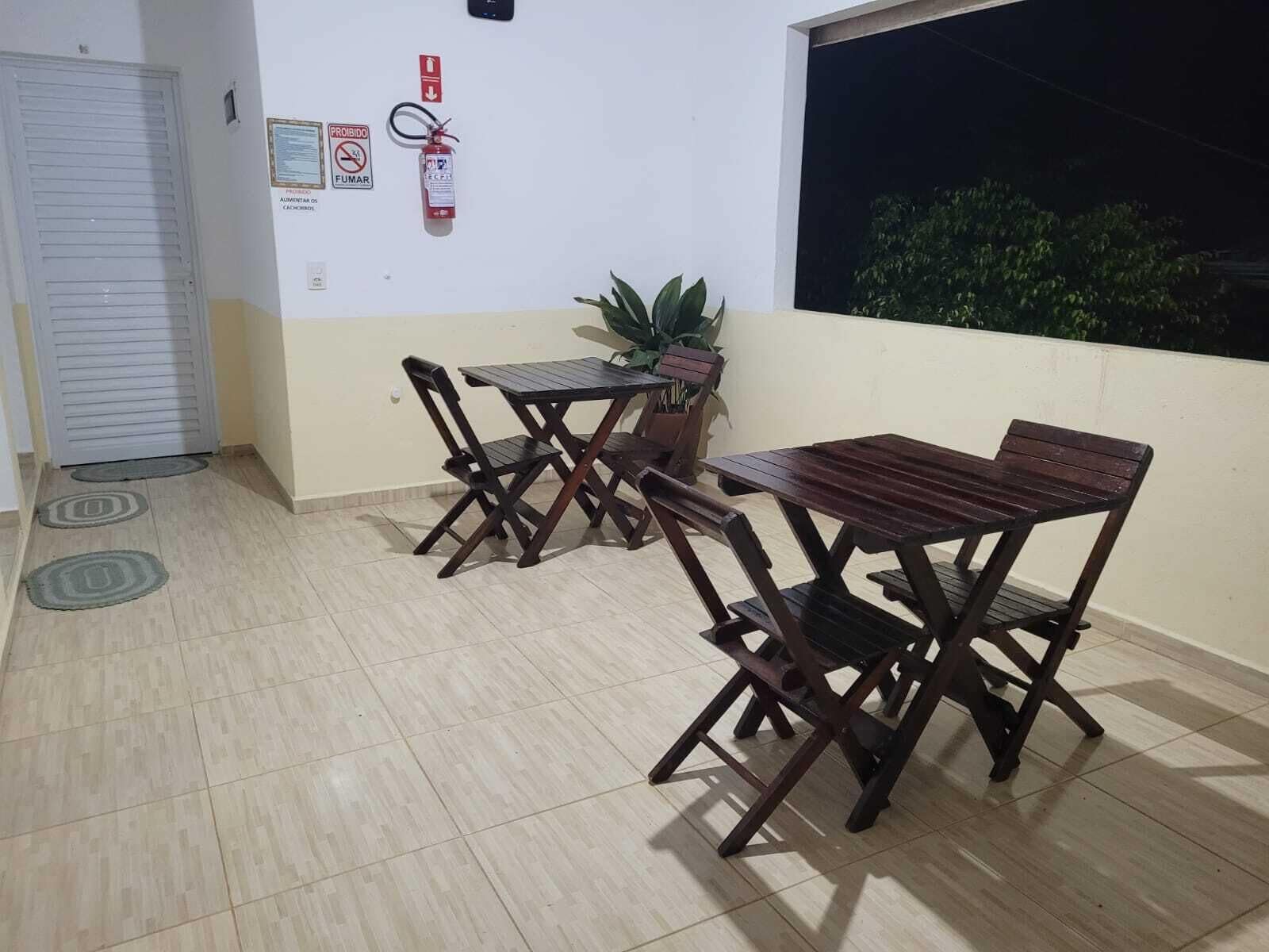 Varanda com mesa e cadeiras de madeira, um vaso de planta e um extintor de incêndio.