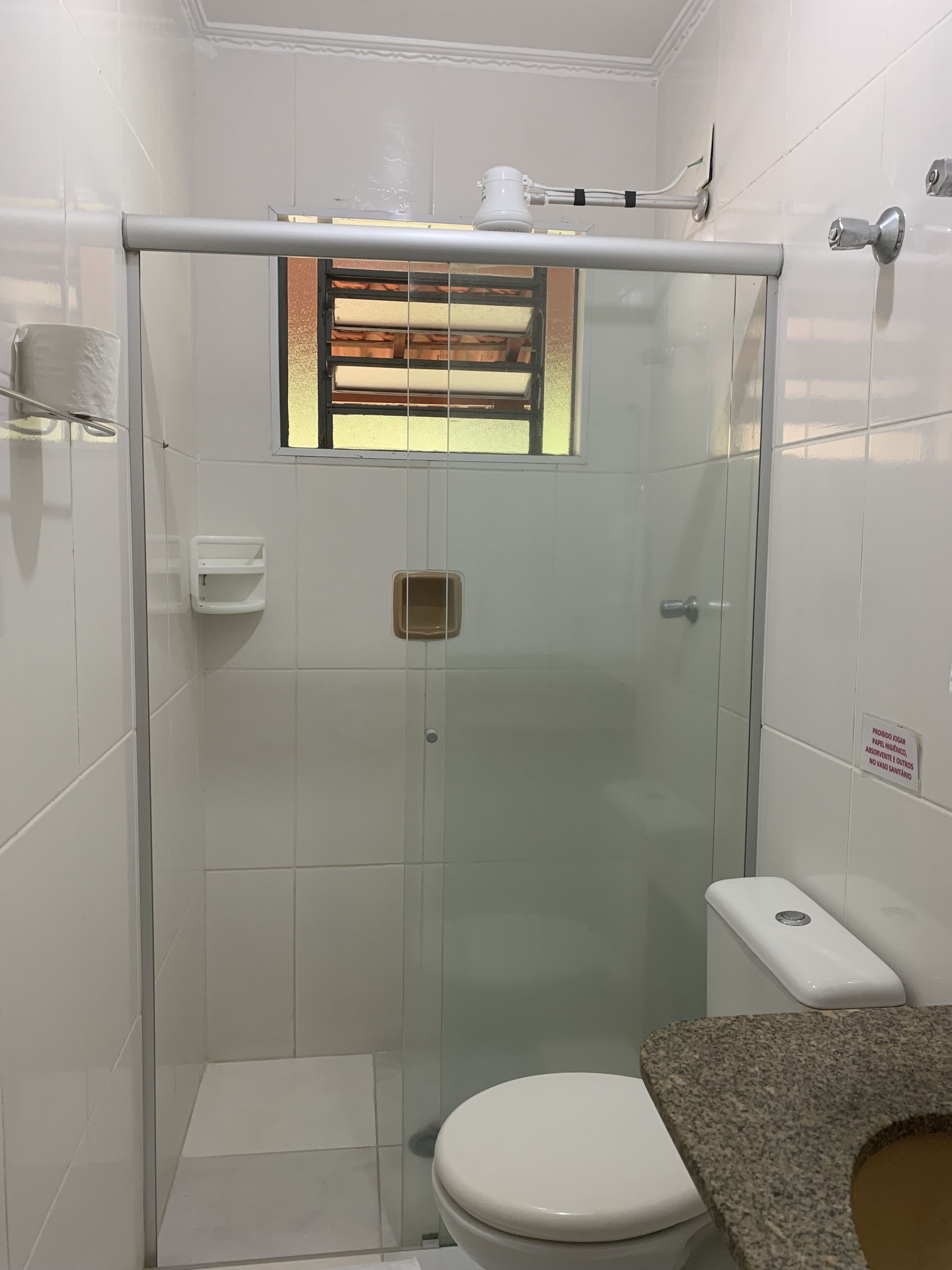 Casa de banho moderna com cabine de chuveiro em vidro, sanita e janela pequena.