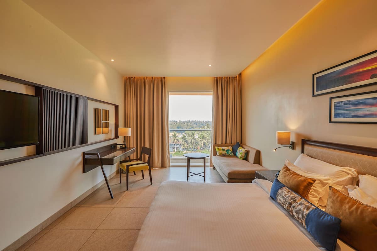 Quarto de hotel com uma cama grande, um sofá, uma escrivaninha e uma televisão.