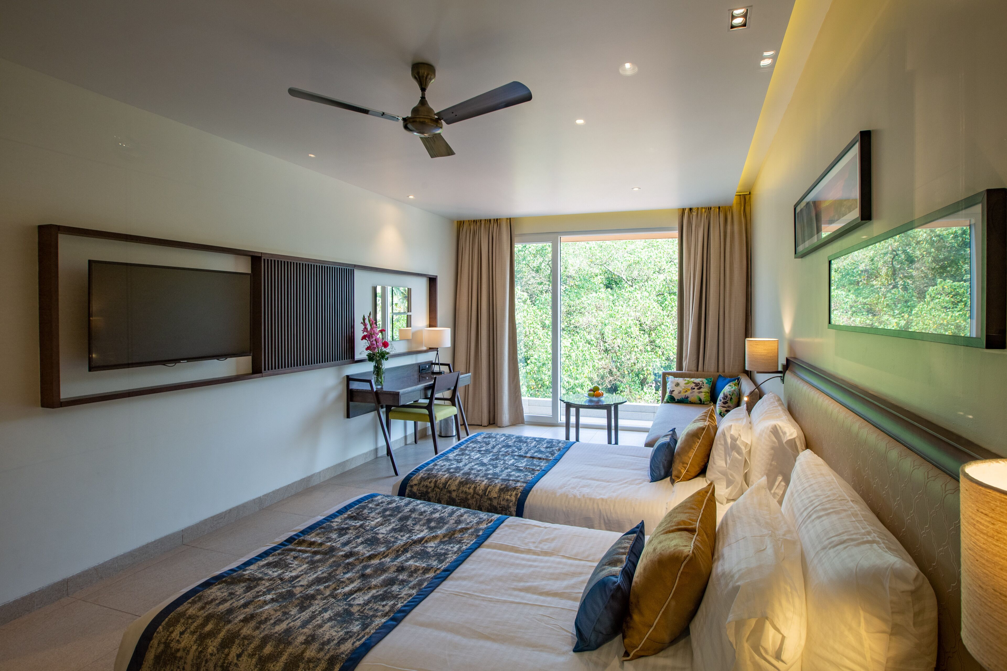 Quarto de hotel com duas camas, televisão de tela plana, escrivaninha com cadeira e janela com cortinas.