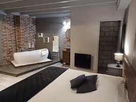 Quarto de hotel moderno com uma cama grande, uma banheira, uma escada de madeira e uma televisão.