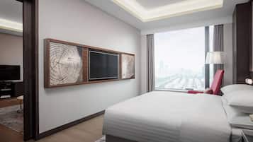Quarto de hotel moderno com uma cama grande, televisão de tela plana na parede, vista para a cidade pela janela e uma cadeira vermelha.