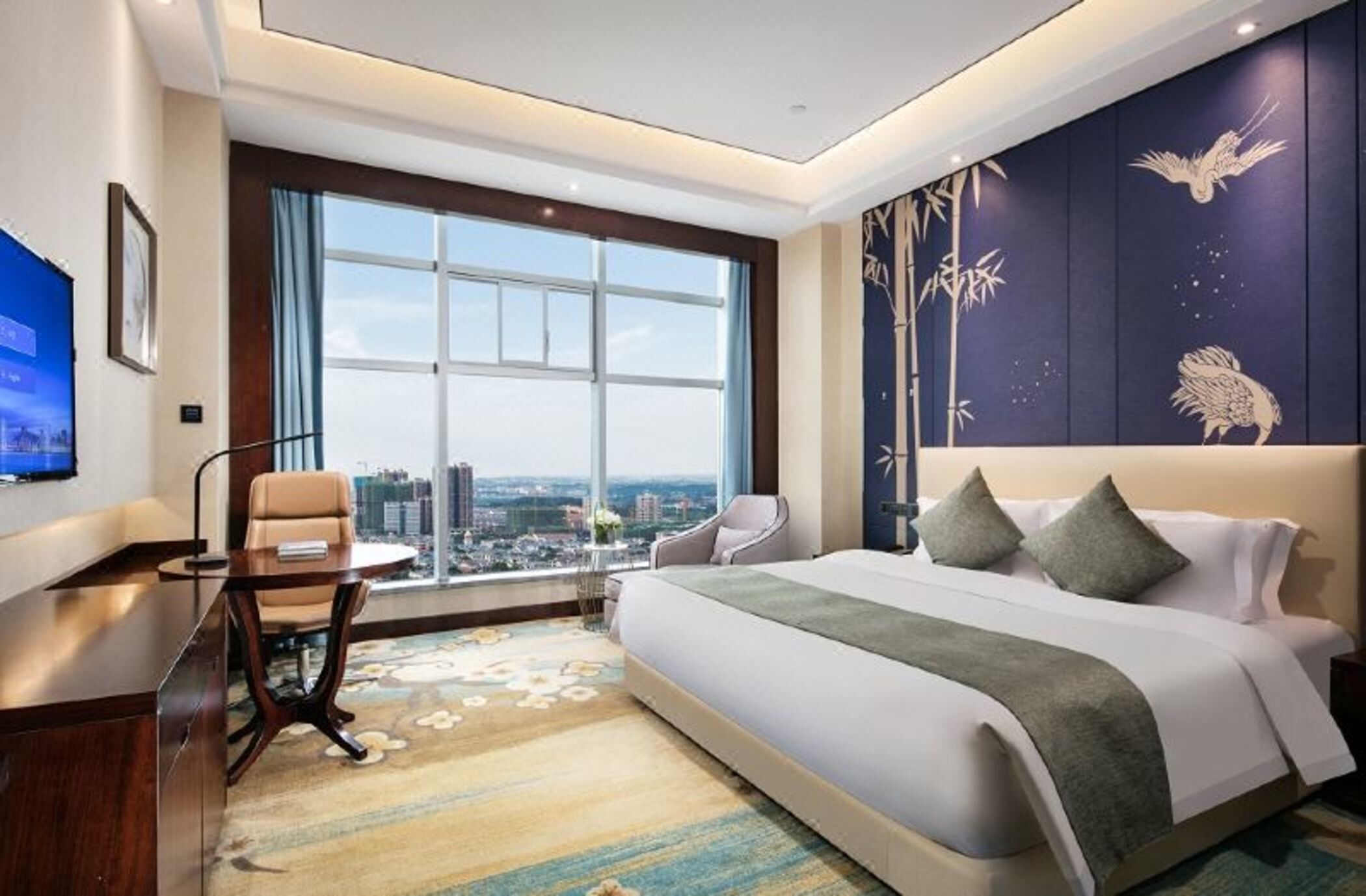 Quarto de hotel com uma cama grande, uma escrivaninha, uma cadeira e vista da cidade através de uma janela ampla.
