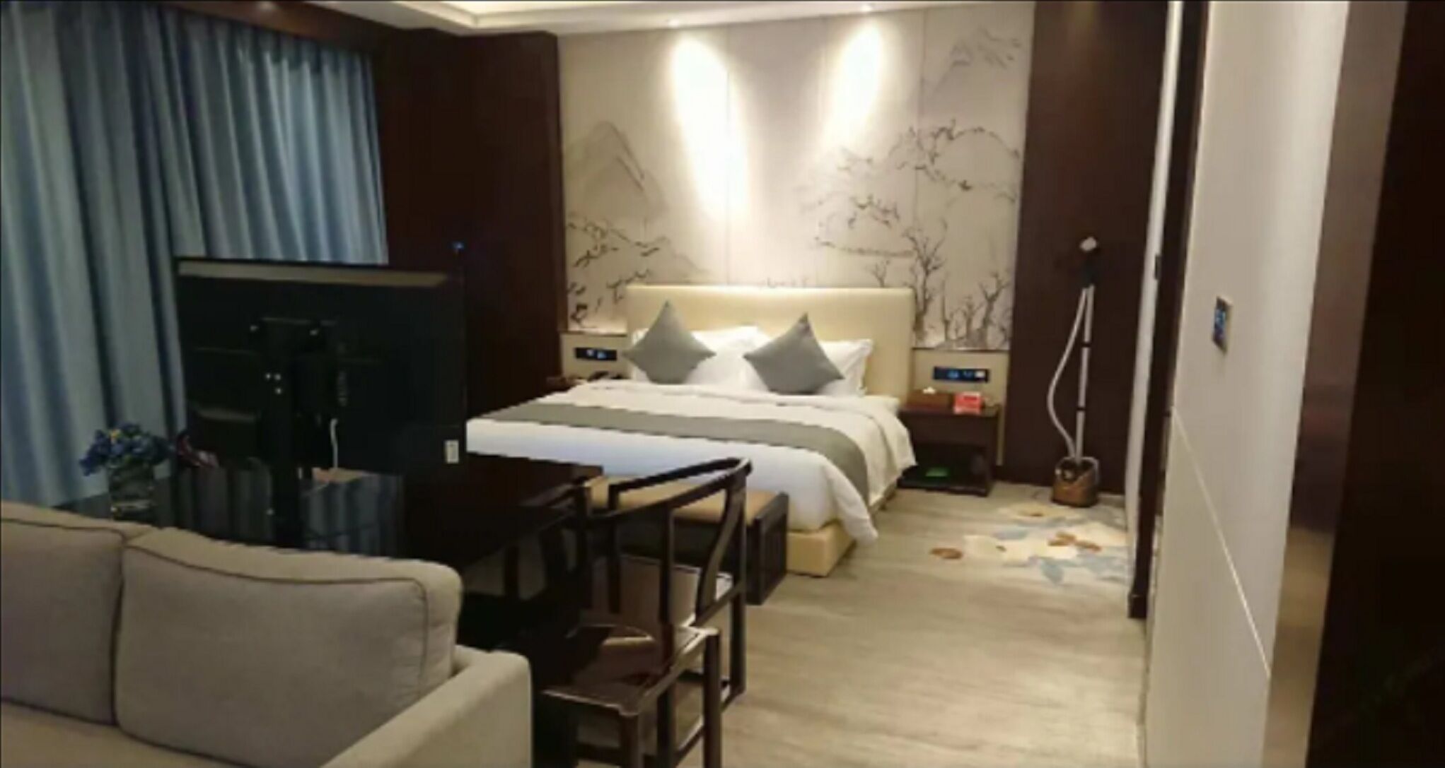 Quarto de hotel moderno com uma cama grande, uma mesa de trabalho, um sofá e uma televisão.