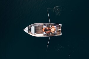 Um pequeno barco de madeira com uma pessoa segurando uma vara de pesca, flutuando em águas calmas.