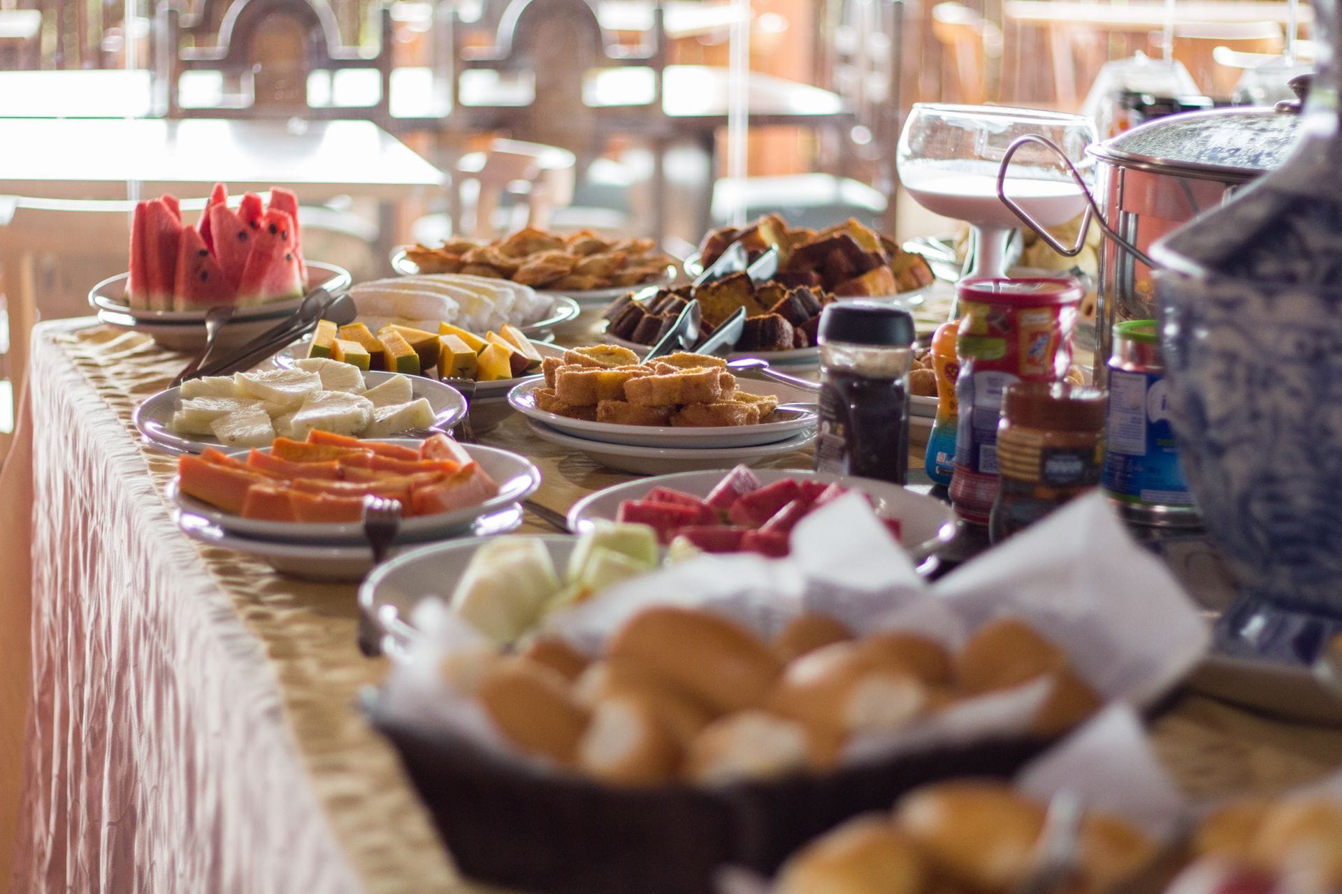 Mesa de buffet com diversos alimentos, incluindo frutas, doces e acompanhamentos.