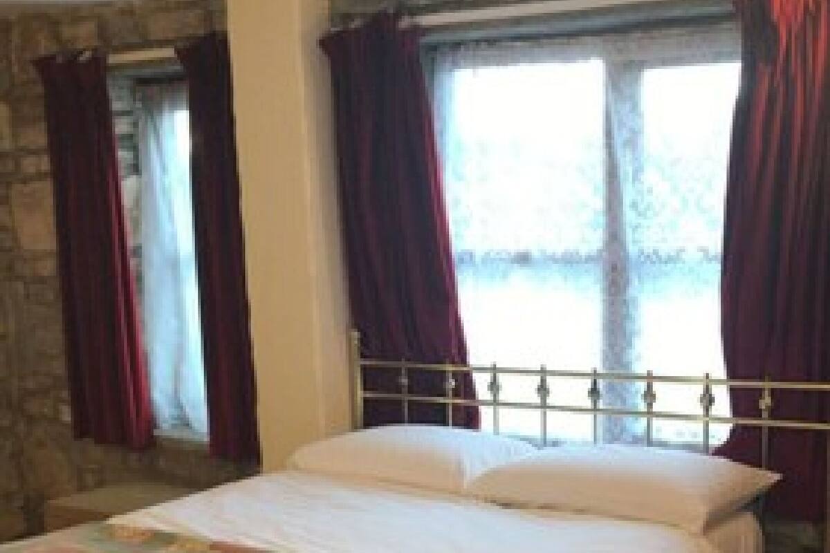 Quarto com cama, janela com cortinas, tapete estampado e parede de pedra.