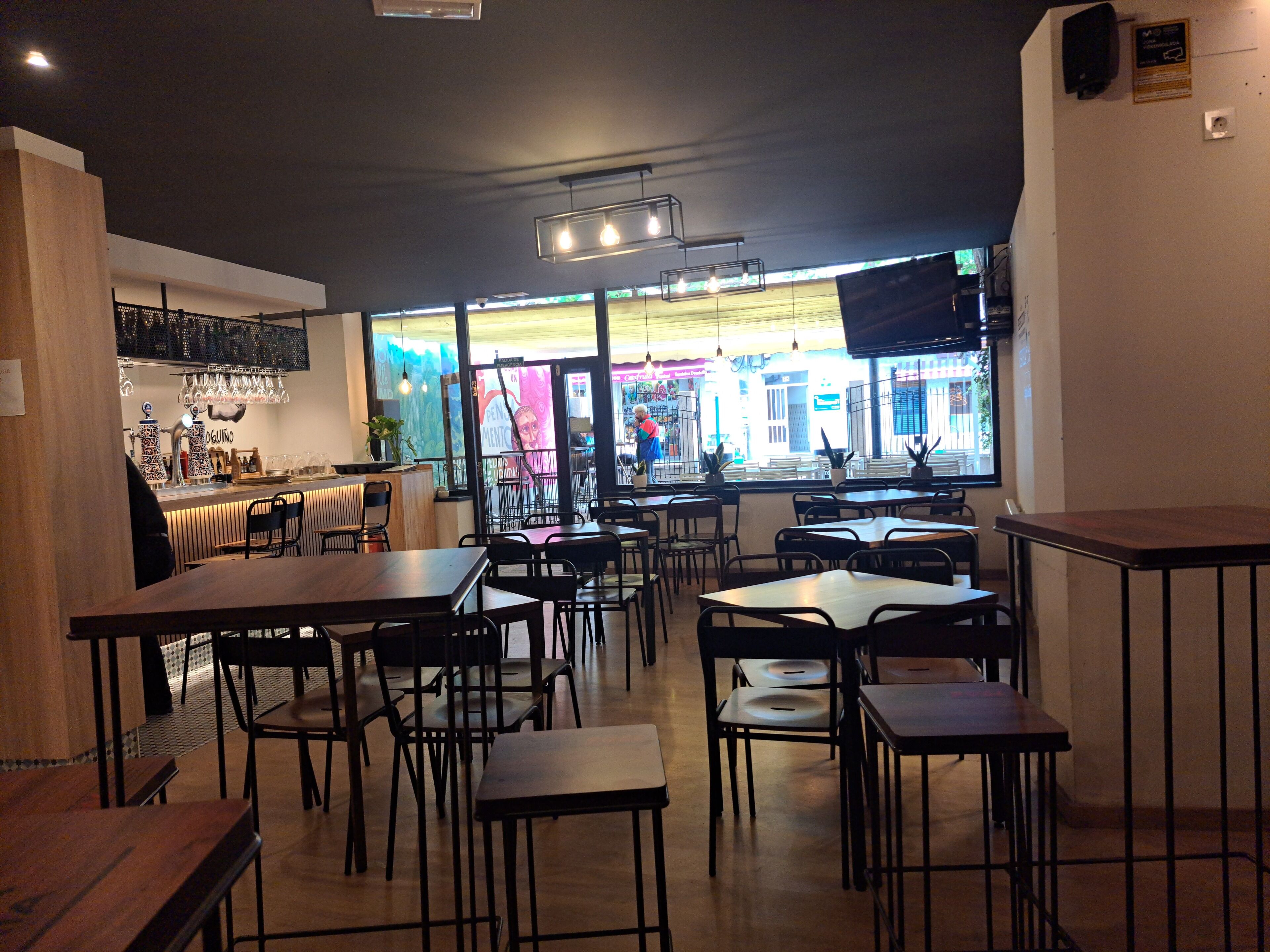 Interior de restaurante com mesas, cadeiras, área de bar e vista para a rua.