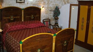 Quarto com parede de pedra, cama de madeira com colcha vermelha, guarda-roupa de madeira e quadro emoldurado na parede.