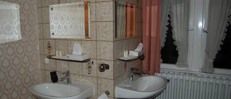 Casa de banho com duas pias, um espelho e uma janela com cortinas.