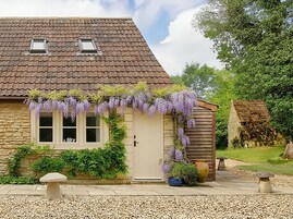Uma casa com fachada de pedra, telhado com telhas e um pequeno jardim com um banco e um vaso de planta.
