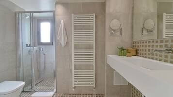 Um banheiro moderno com box de vidro, um porta-toalhas branco, um espelho grande e uma banheira branca.
