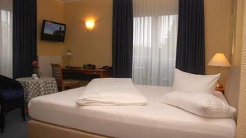 Quarto de hotel com uma cama, escrivaninha, cadeira, televisão e abajur.