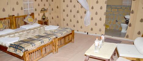 Quarto com cama de madeira, mesa de cabeceira, pequena mesa com garrafas e um banheiro visível por uma porta aberta.