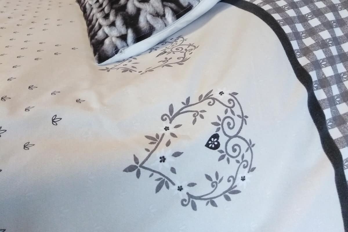 Uma cama com travesseiro estampado e manta xadrez.