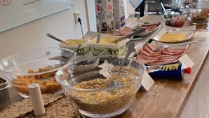 Buffet com diversos alimentos e um quadro branco com anotações manuscritas ao fundo.