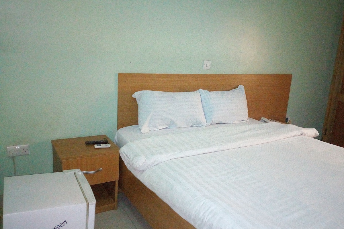 Uma cama de solteiro com cabeceira de madeira, roupa de cama branca e mesa de cabeceira com um controle remoto.
