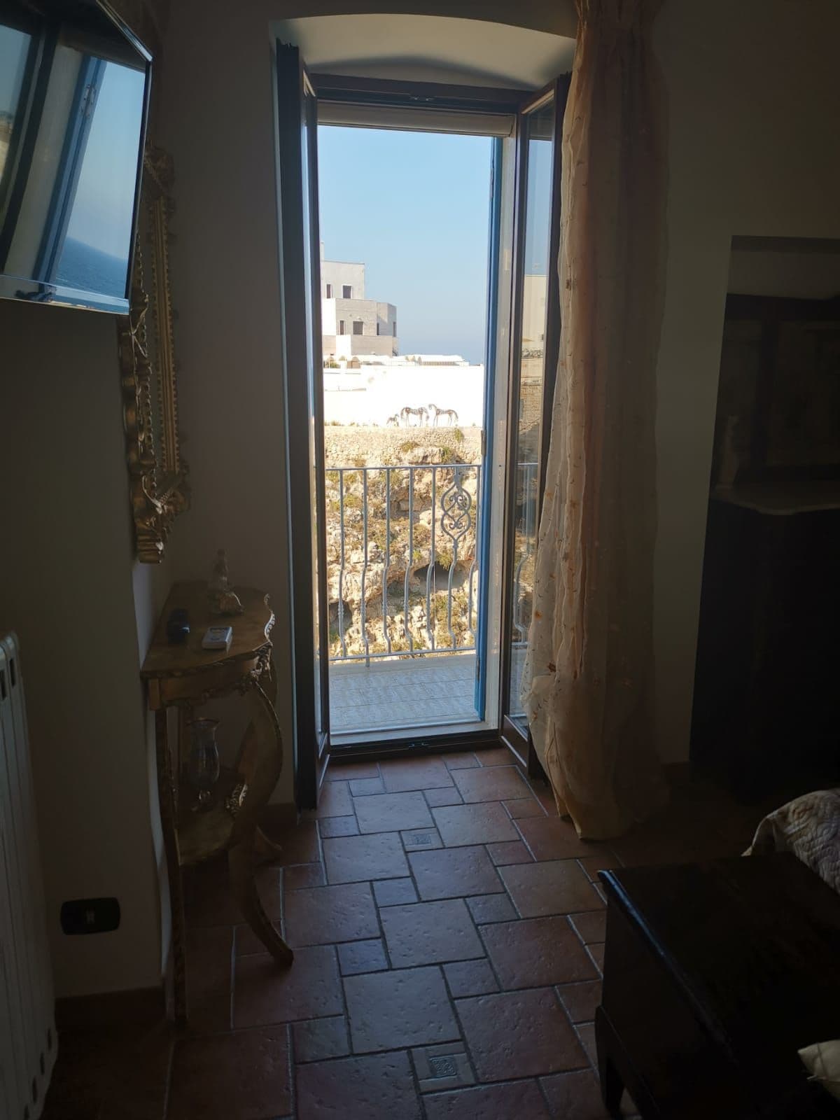 Quarto com vista para o mar através de uma porta de vidro deslizante, uma pequena mesa com um vaso e uma cama.