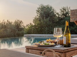 Mesa de madeira com uma garrafa de vinho, duas taças e um prato de comida à beira da piscina.