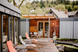 Um deck moderno ao ar livre com pérgola de madeira, área de estar e entrada com porta de vidro.