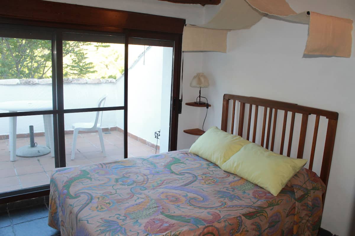 Quarto com cama, uma cadeira, abajur e vista para área externa através de uma porta de correr.