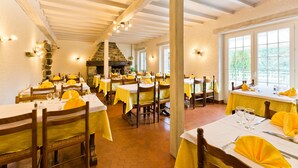 Um restaurante com várias mesas preparadas para refeições, com toalhas de mesa amarelas e cadeiras de madeira.