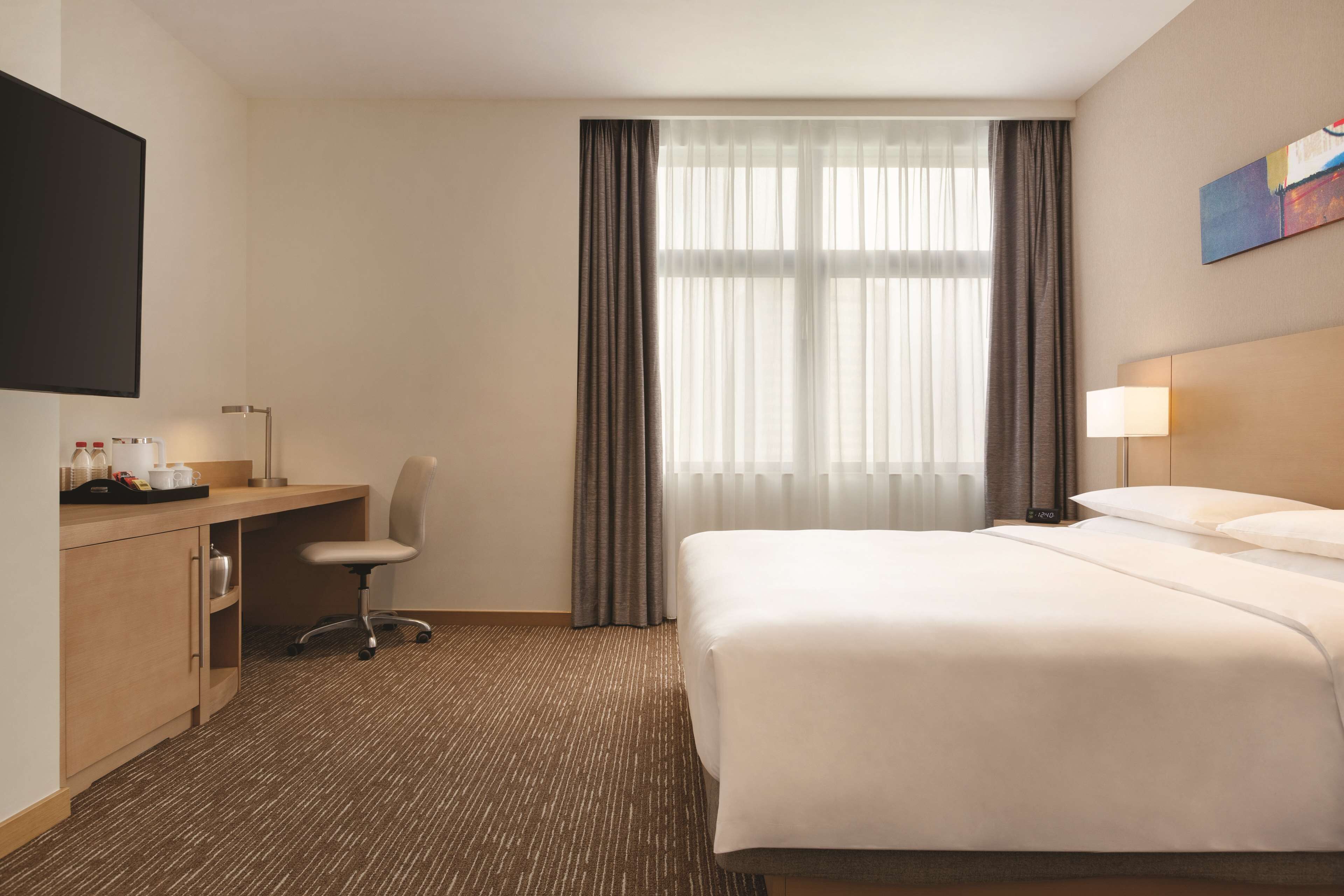 Quarto de hotel com cama, escrivaninha, cadeira e televisão na parede.
