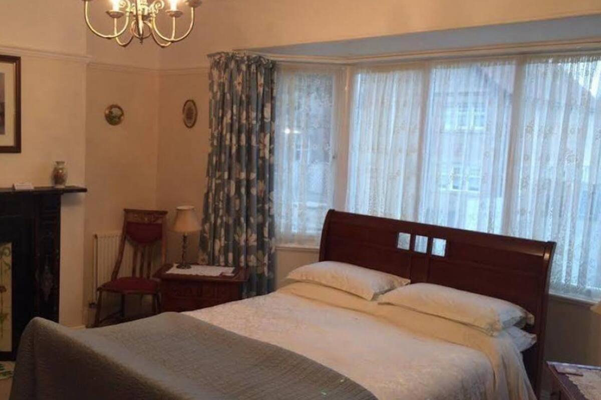 Quarto com cama, cadeira, mesa de cabeceira, lareira e janela com cortinas.