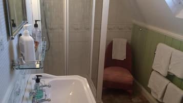 Casa de banho com chuveiro, lavatório com dispensador de sabão e uma cadeira.