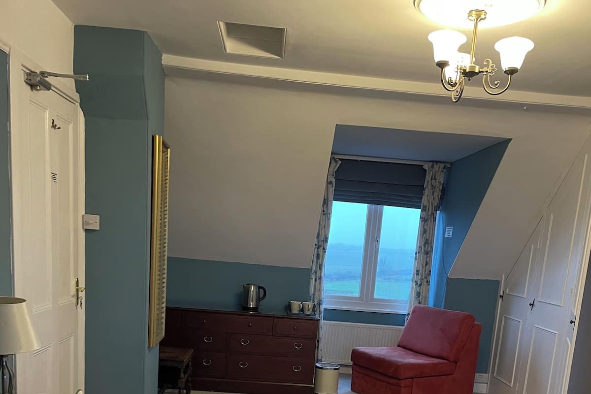 Quarto com cama, uma cadeira vermelha, cômoda e janela com vista.