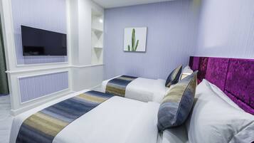 Quarto de hotel com duas camas, televisão, obra de arte de cacto e cabeceira roxa.
