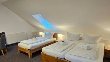 Quarto de hotel com duas camas de solteiro, uma escrivaninha, uma cadeira e um claraboia.