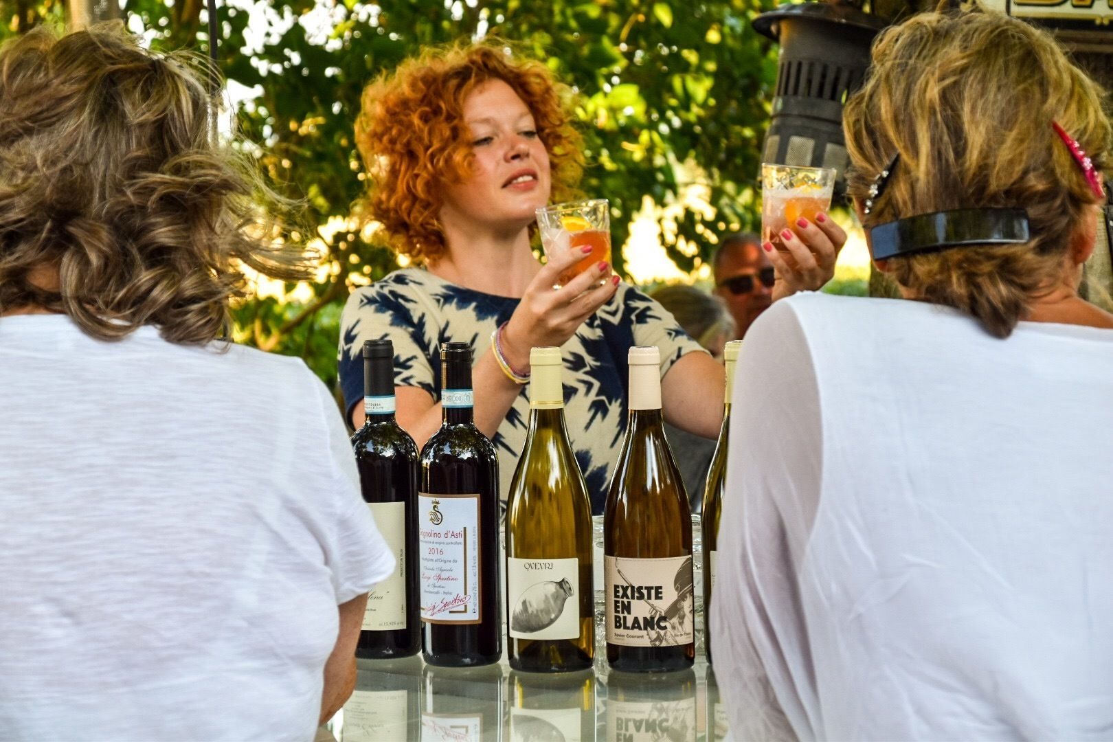 Um grupo de pessoas em um evento de degustação de vinhos, com diversas garrafas sobre a mesa.