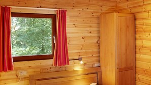 Quarto de cabana de madeira com cama, mesa de cabeceira, janela com cortinas e guarda-roupa.