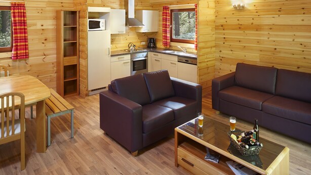 Interior acolhedor de uma cabana com área de jantar, dois sofás, uma mesa de centro e cozinha.
