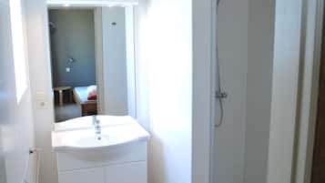 Casa de banho com lavatório branco, espelho e cabine de duche.