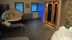 Um spa moderno com banheira aquecida, um espaço de estar confortável com almofadas e vista para o exterior através de uma janela.