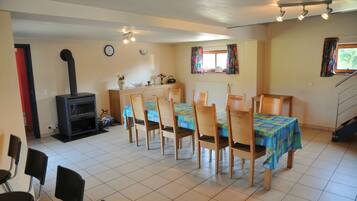 Uma sala de jantar com uma mesa posta para quatro pessoas, uma lareira a lenha e uma janela com cortinas.